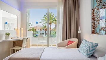 Quarto de hotel com cama, escrivaninha, cadeira e varanda com vista para palmeiras e edifícios.
