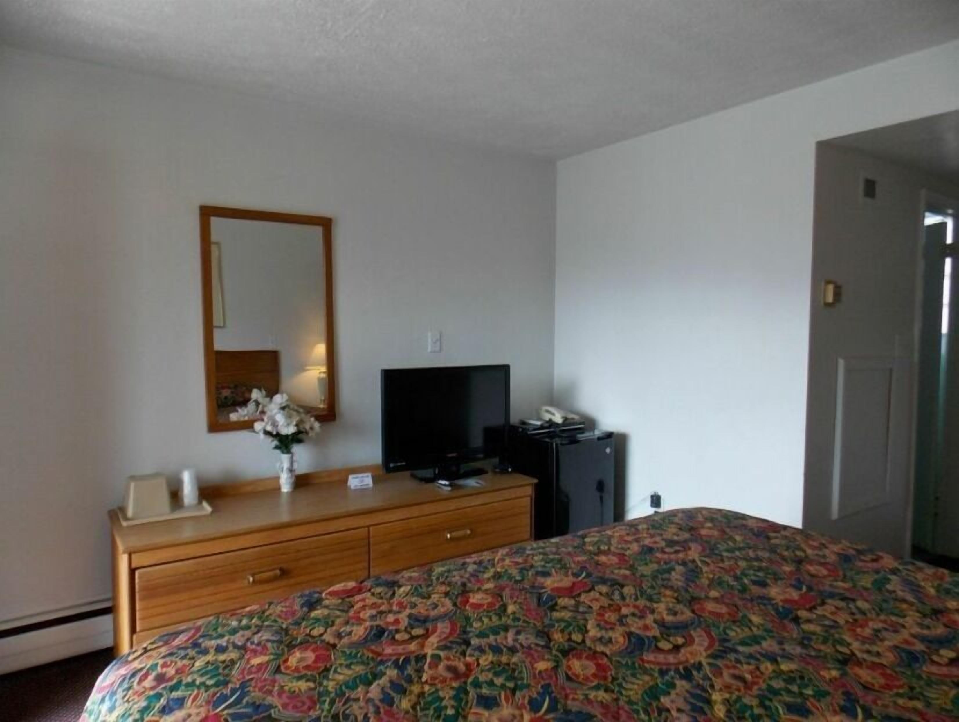Quarto de hotel com cama, penteadeira, televisão, espelho e porta.