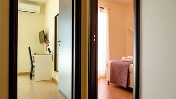 Quarto de hotel com cama, escrivaninha e cadeira. Há uma televisão na parede e uma janela com cortinas.
