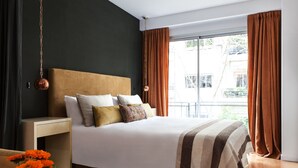 Quarto moderno com uma cama grande, mesa de cabeceira e janela com cortinas.