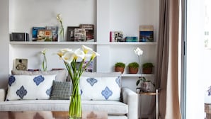 Uma sala de estar com sofá, mesa de centro e estante com livros e objetos decorativos.