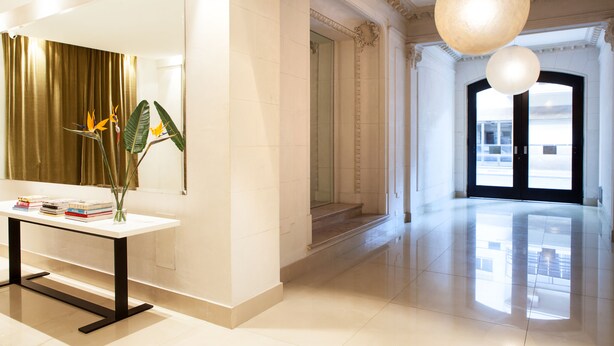 Um saguão de hotel moderno com uma recepção branca, um espelho grande e vista para o exterior através de uma porta de vidro.