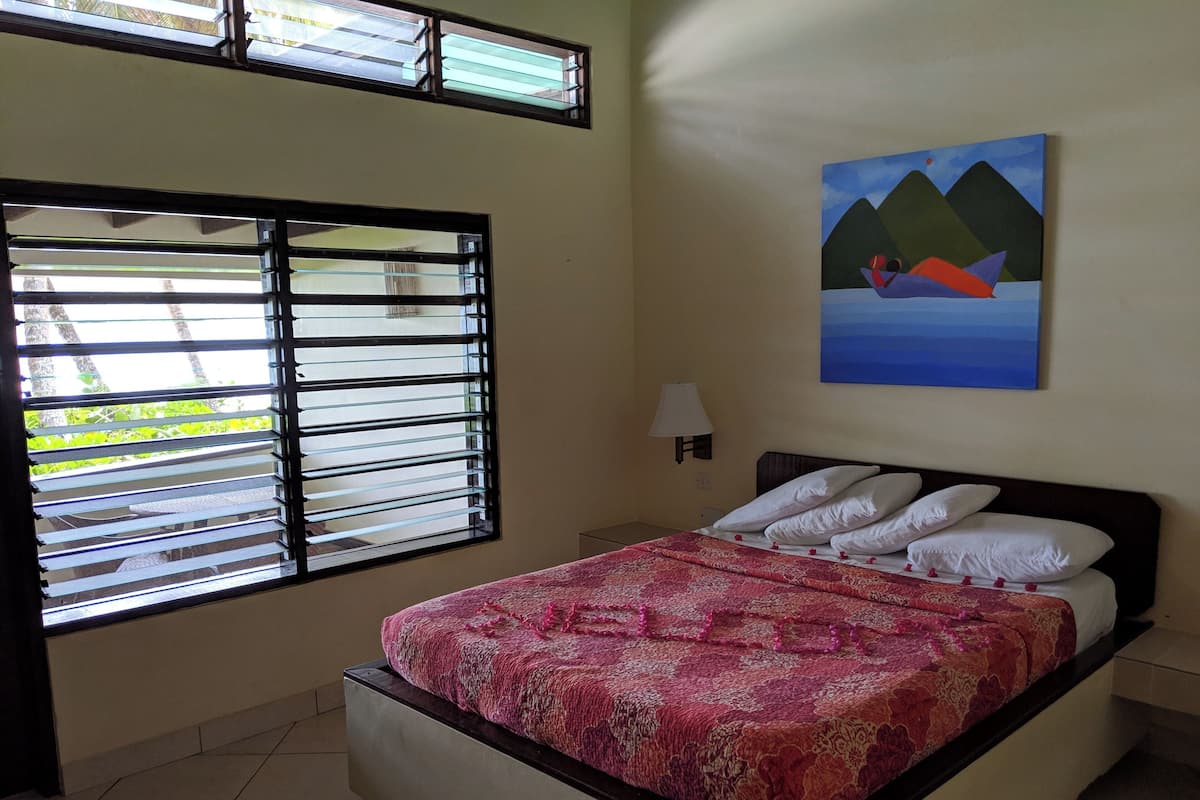 Quarto com cama, janela com persianas, luminária na parede e um quadro.