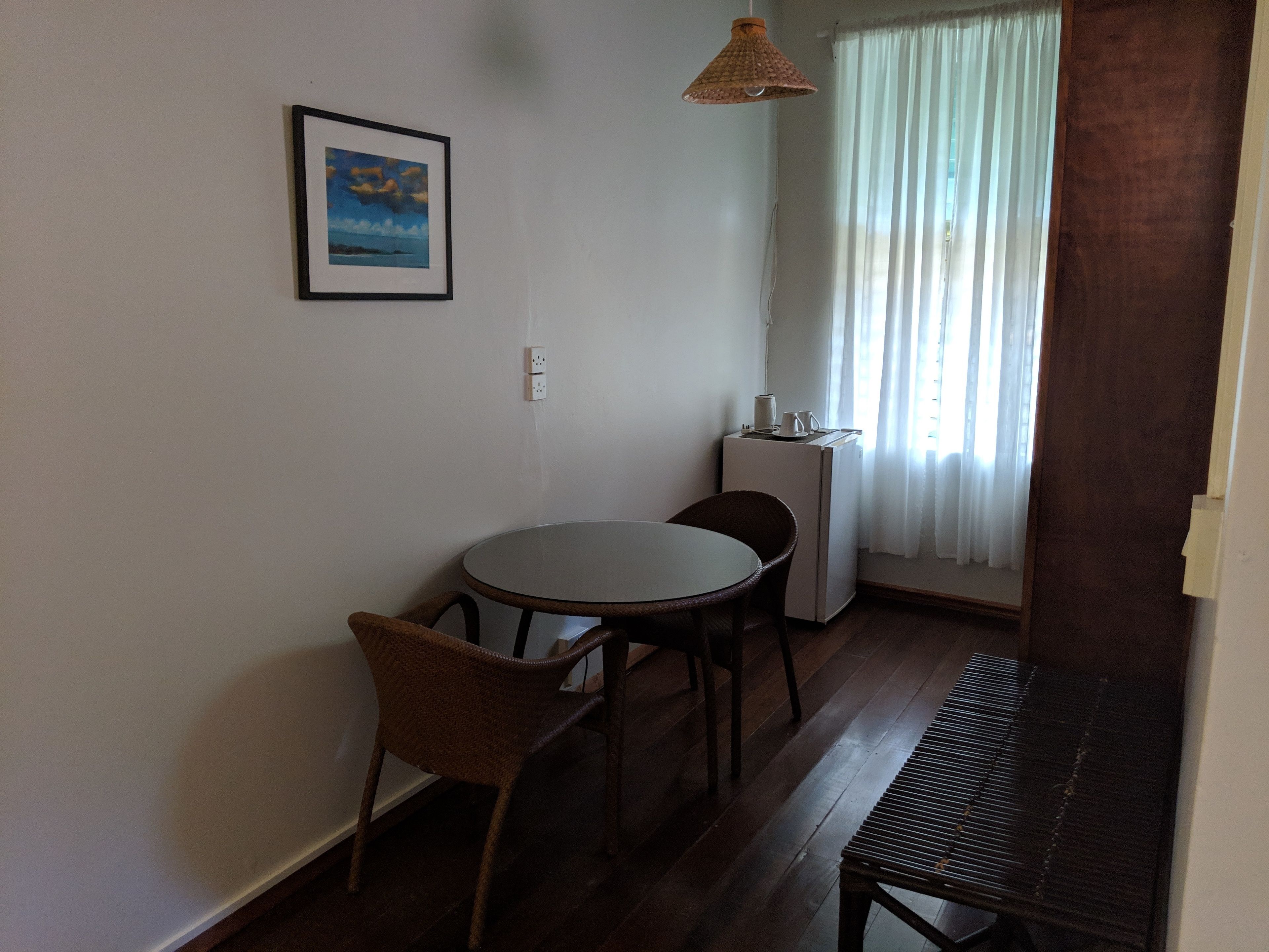 Uma pequena área de refeições com uma mesa redonda, duas cadeiras, uma geladeira e um lustre.