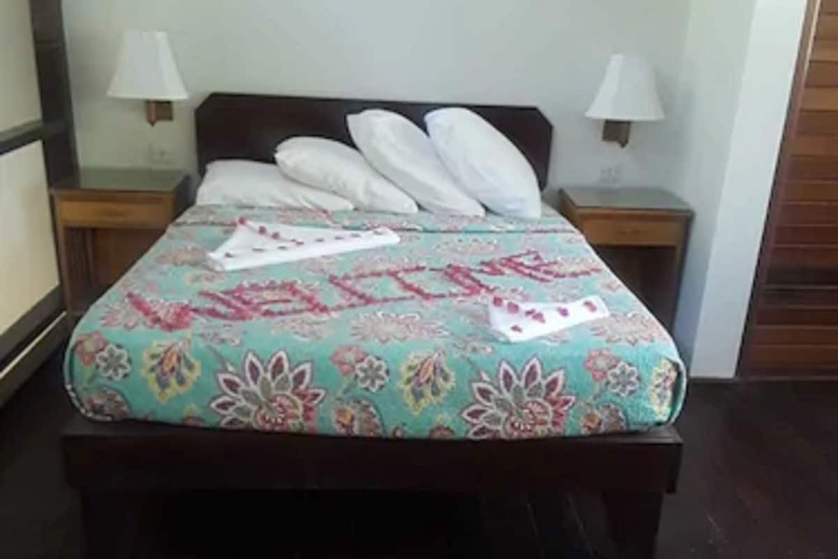 Uma cama com colcha florida, duas mesas de cabeceira com abajures e um chão de madeira escura.