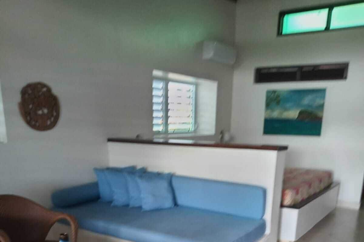 Uma sala de estar com um sofá azul, uma mesa de madeira e uma parede branca com um relógio e um quadro.