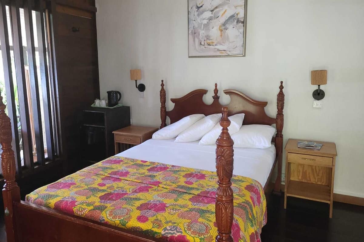 Cama bem arrumada com colcha florida, cabeceira de madeira e duas mesas de cabeceira com abajures.