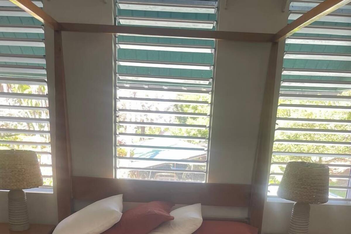 Quarto de hotel com uma cama grande, duas mesas de cabeceira e uma janela com persianas horizontais.