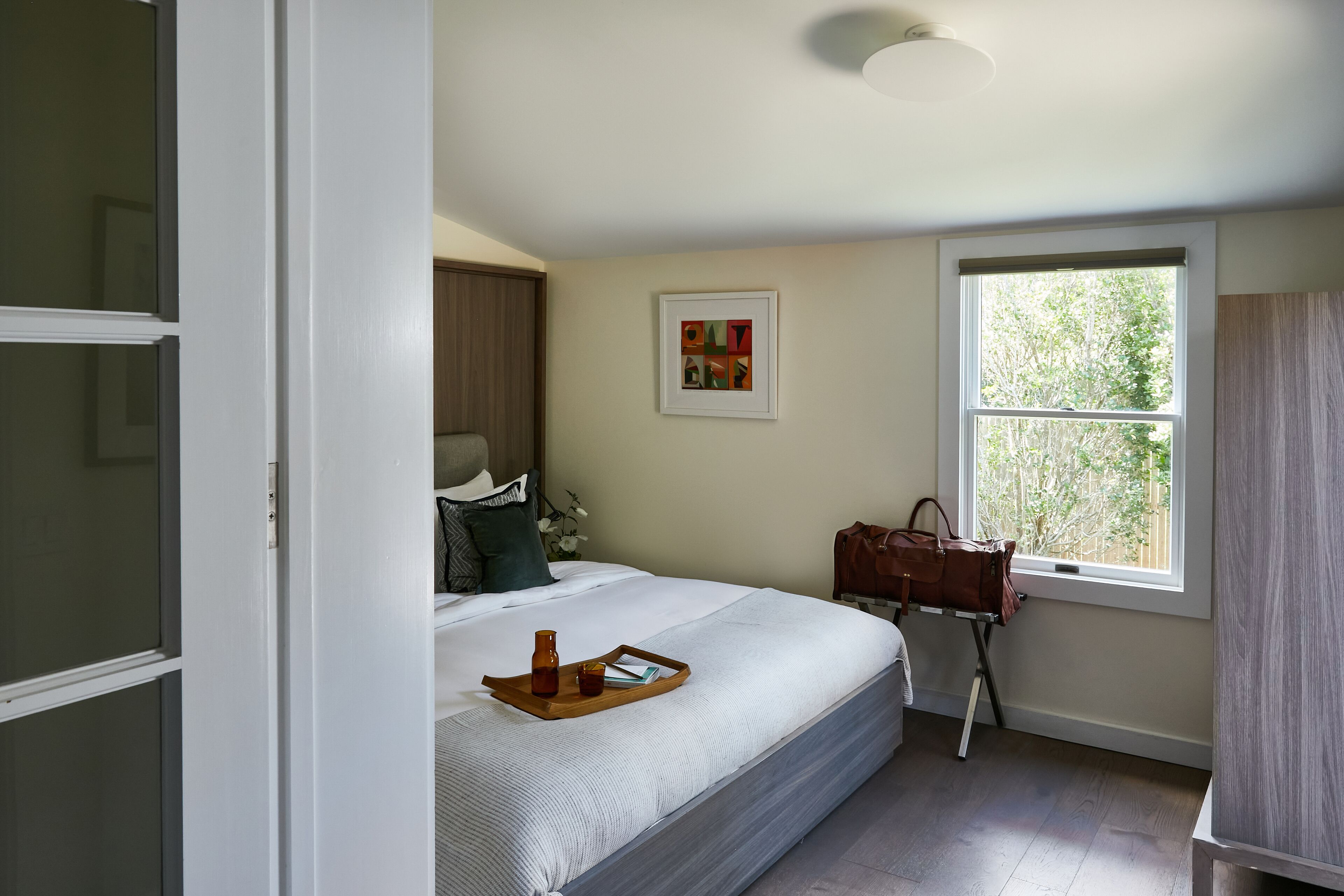 Quarto com cama, janela, porta e quadro fixado na parede.