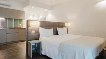 Quarto de hotel moderno com uma cama grande, mesas de cabeceira, televisão integrada e um espaço com cozinha compacta.