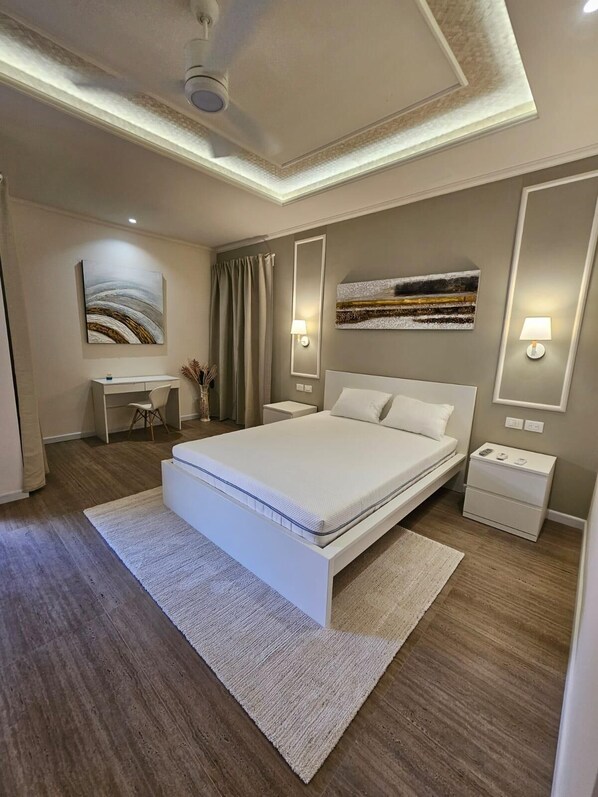 Quarto moderno com cama grande, mesas de cabeceira, escrivaninha e obras de arte nas paredes.