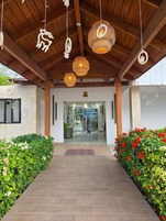 Uma entrada coberta com luminárias pendentes, um caminho e uma porta de vidro que dá acesso ao interior.