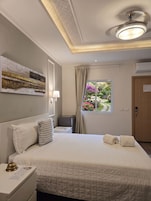 Quarto de hotel com cama, mesa de cabeceira, abajur, janela com vista para um jardim e uma porta.