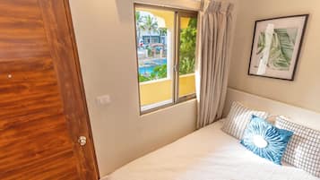 Quarto com porta de madeira, janela com cortinas, cama com roupa de cama estampada e quadro na parede.