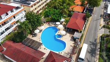 Piscina cercada por área de estar externa e guarda-sóis, com edifícios ao fundo.