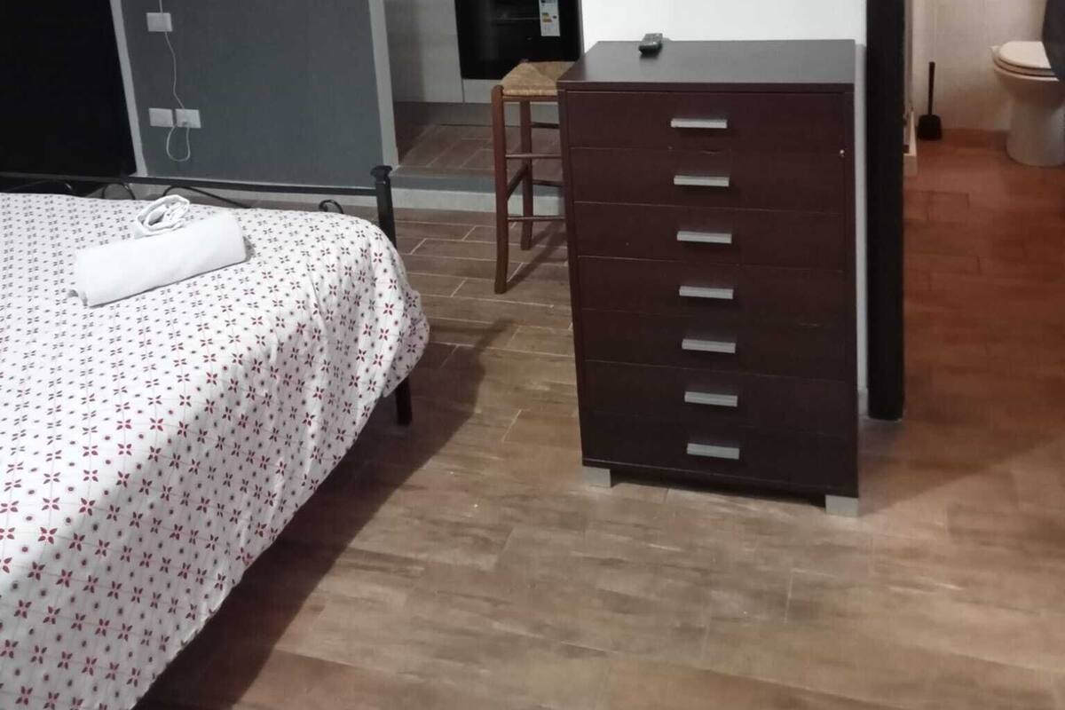 Quarto com cama, cômoda e vista para a cozinha.