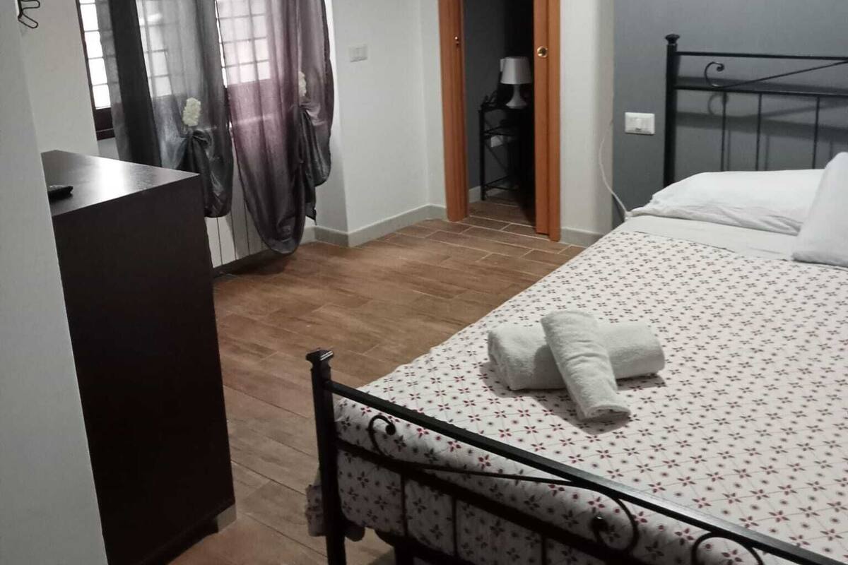Quarto com cama, escrivaninha e porta que dá para outro cômodo.
