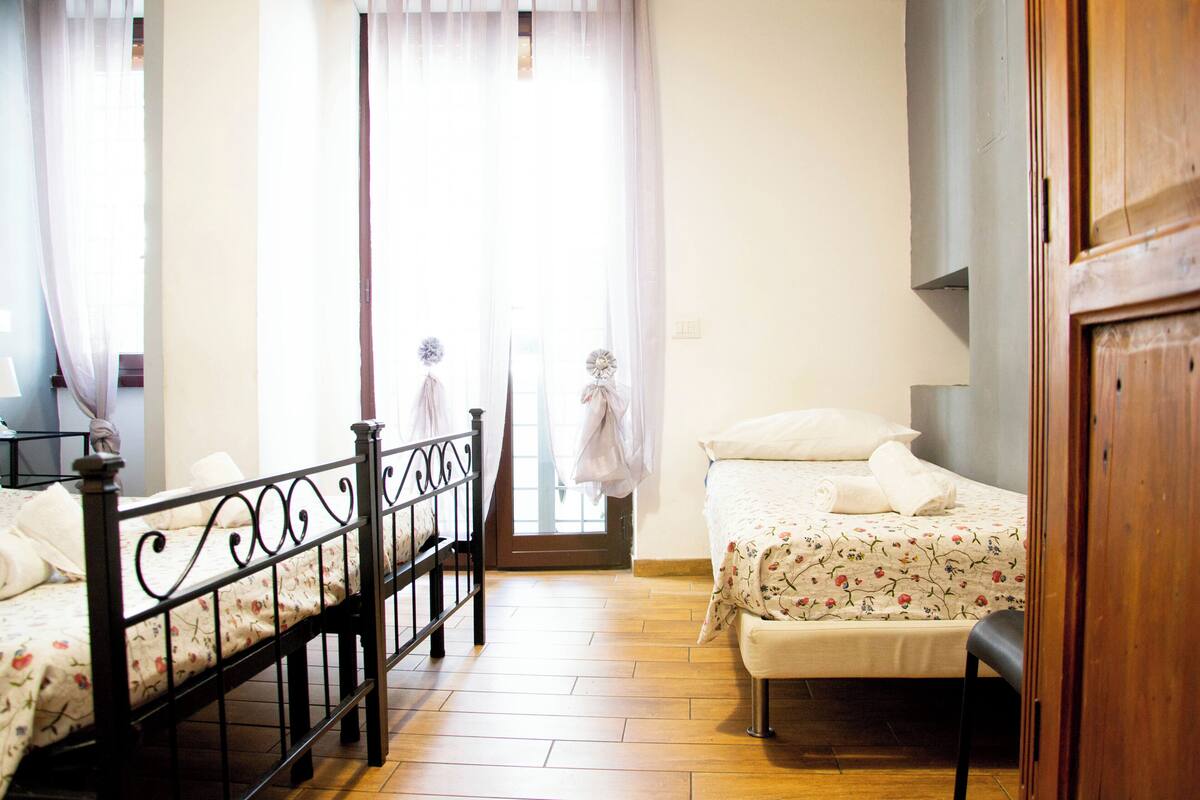 Quarto com duas camas de solteiro, piso de madeira e porta que dá para uma varanda.