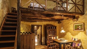 Um interior rústico com escada de madeira, sala de jantar com mesa e cadeiras, e cozinha com armários e luminária pendente.