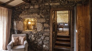 Um quarto aconchegante com parede de pedra, uma poltrona xadrez, uma luminária e uma escada que leva a outro espaço.
