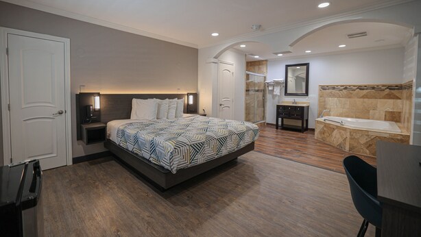 Quarto moderno com uma cama grande, toucador com espelho, área de chuveiro e escrivaninha.