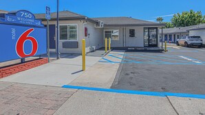 Um motel com um grande letreiro azul, sinal de vaga para deficientes e entrada acessível a cadeirantes.