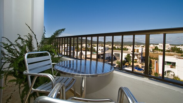Uma varanda com uma mesa redonda e duas cadeiras, com vista para uma área residencial com casas e um céu azul límpido.