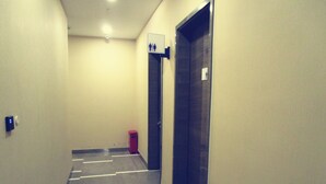 Corredor com piso coberto por carpete, uma lixeira e duas portas, uma identificada para homens e outra para mulheres.