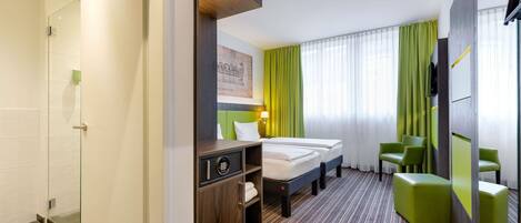 Quarto de hotel com cama, escrivaninha, cadeira e área de chuveiro.