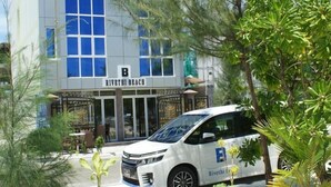 Um carro branco estacionado em frente à Praia Rivethi, um edifício com grandes janelas e uma placa sobre a entrada.