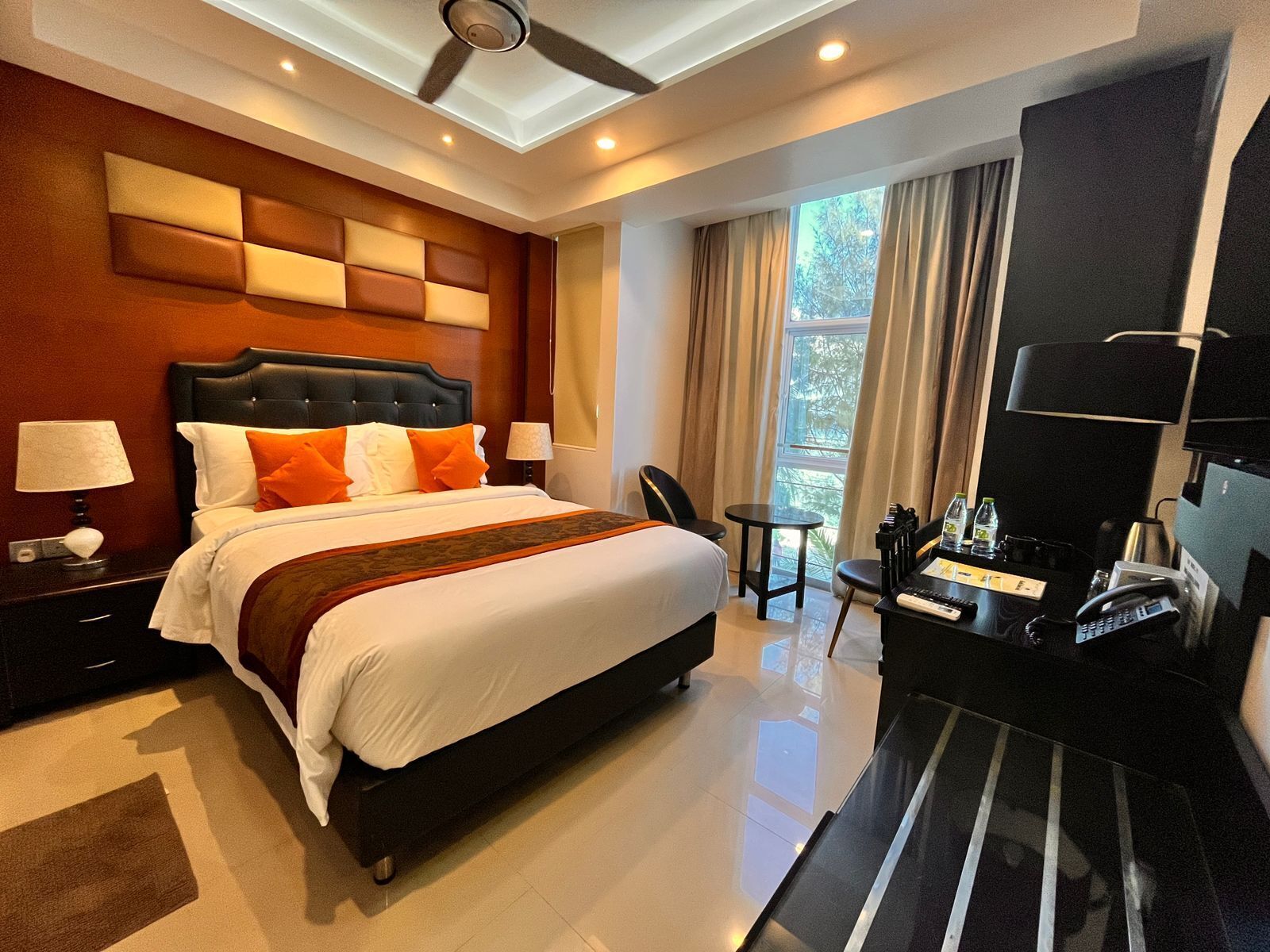 Quarto de hotel com uma cama grande, uma escrivaninha, uma cadeira e um ventilador de teto.