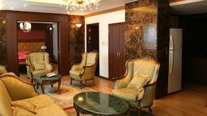 Uma sala de estar ampla com um lustre, duas poltronas, um sofá e uma mesa de centro de mármore.