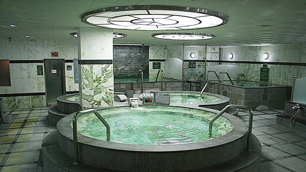 Uma área de spa com duas banheiras de hidromassagem circulares, uma parede de mármore e um teto com luminárias circulares.