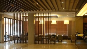 Um lobby moderno com piso refletivo, área de estar com mesas e cadeiras, e um painel de madeira decorativo.
