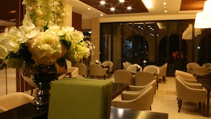 Um hall de hotel com um grande arranjo floral, área de estar e vista pelas portas de vidro.