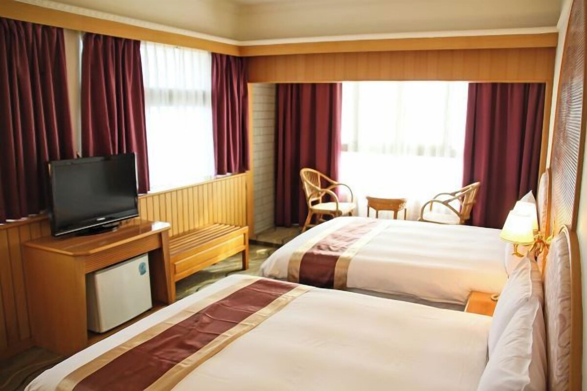 Quarto de hotel com duas camas, televisão, pequena escrivaninha e uma cadeira.