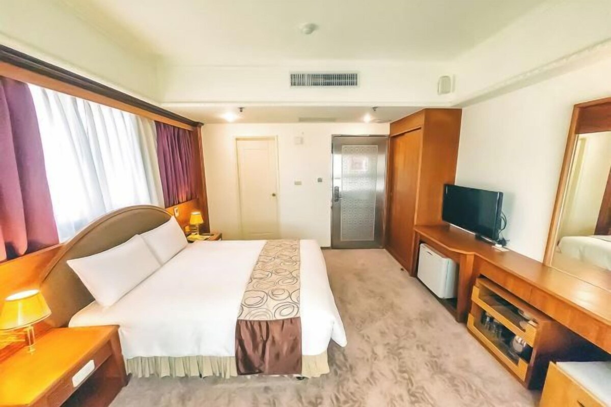 Quarto de hotel com uma cama, televisão, escrivaninha e espelho.