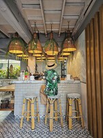 Interior de restaurante com área de bar, luminárias de vime penduradas e piso estampado.
