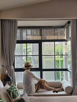 Quarto com uma grande janela e um sofá, uma mesinha e um abajur.
