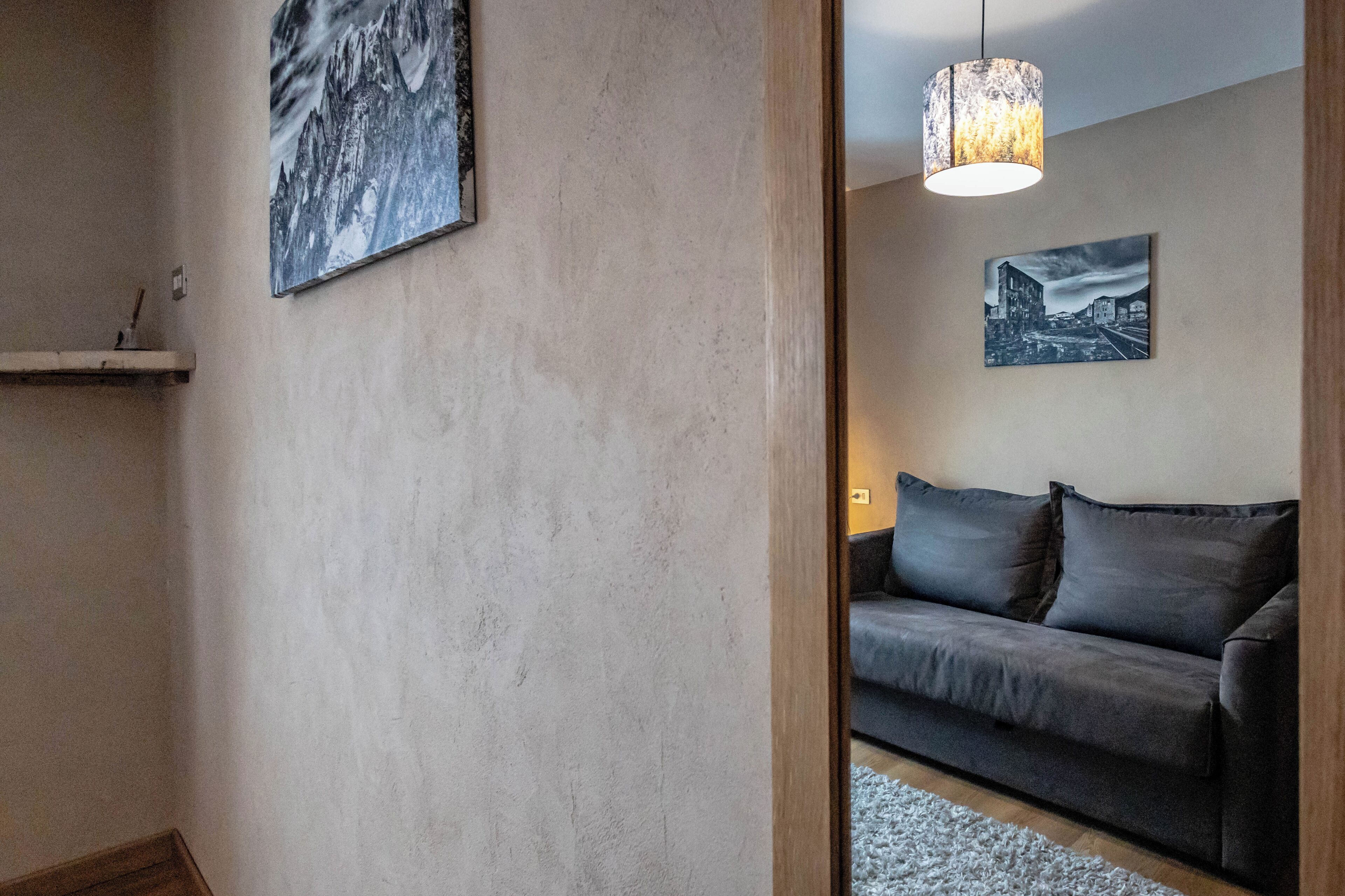 Um quarto com um sofá cinzento, uma luminária pendente e duas molduras na parede.
