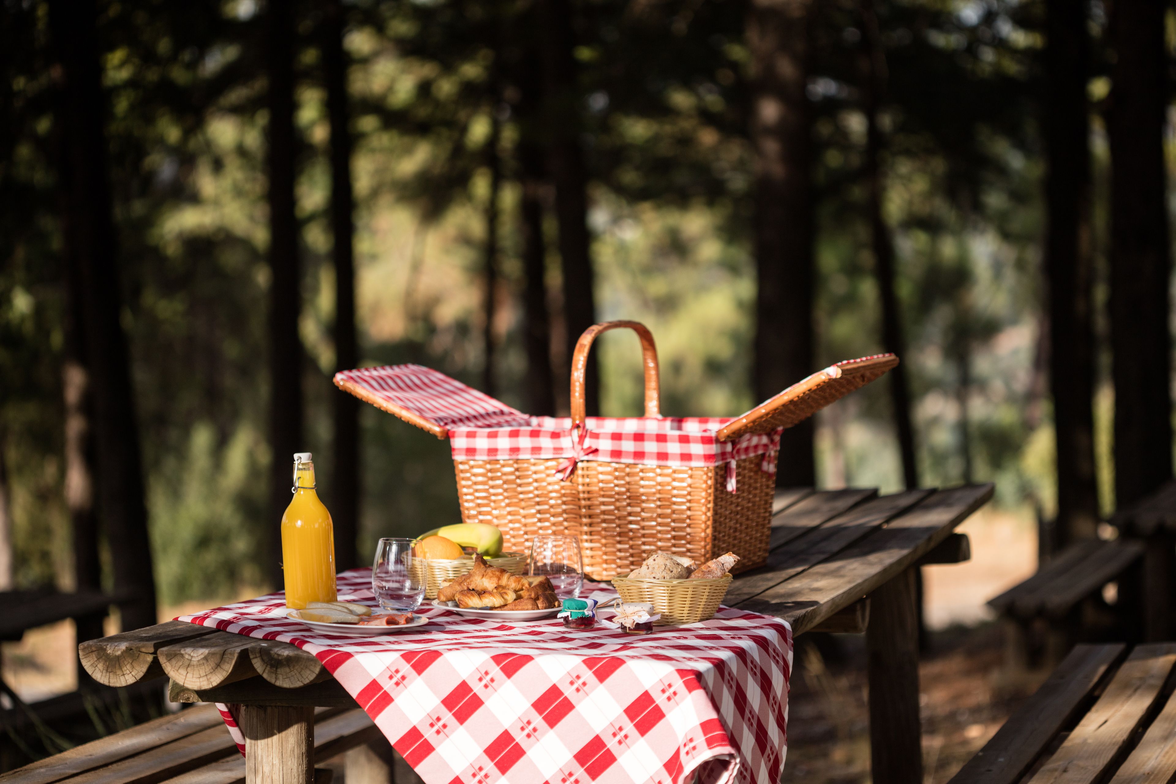 Uma cesta de piquenique com frutas, pão e uma garrafa sobre uma mesa de madeira em uma floresta.