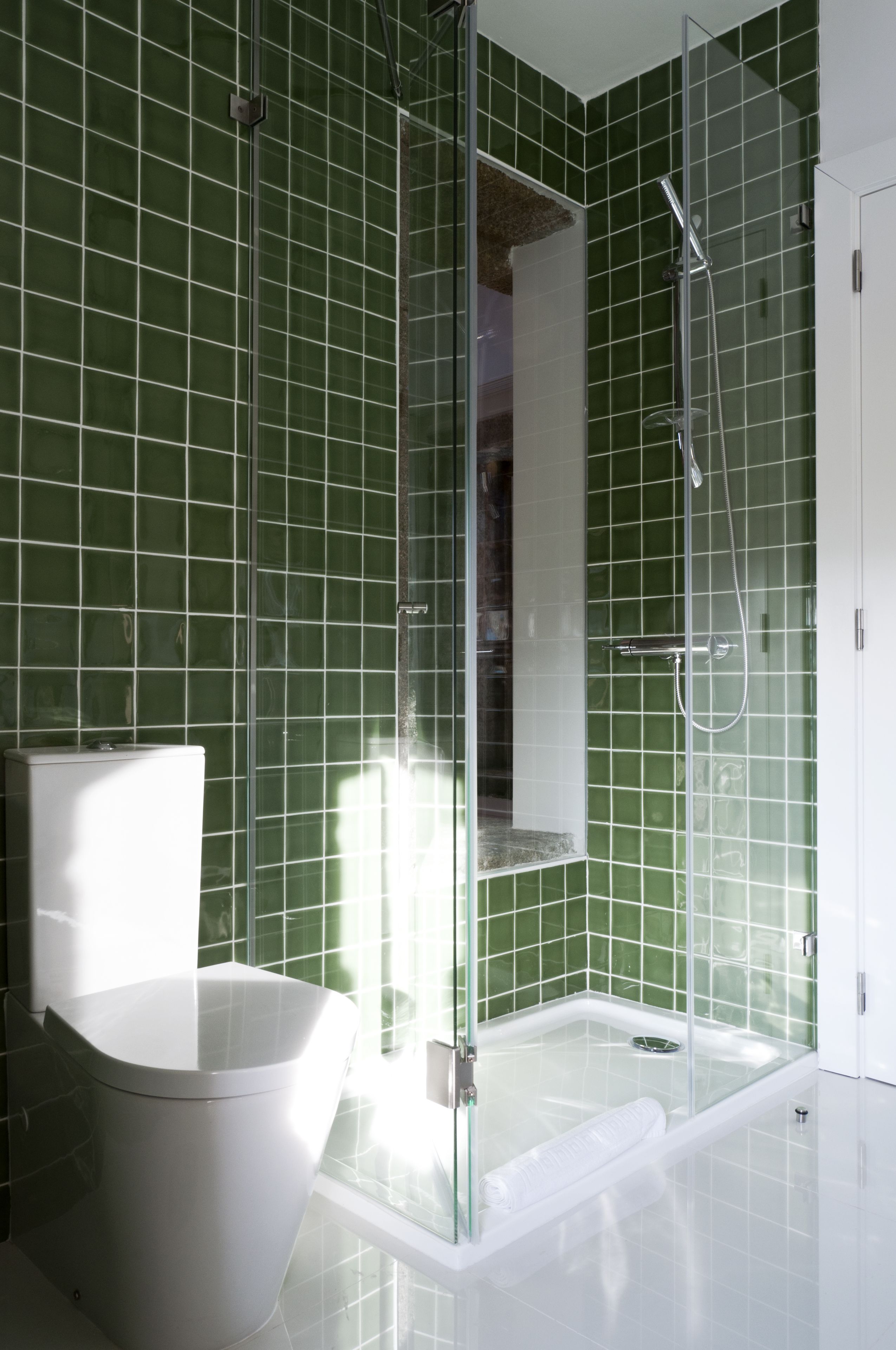 Casa de banho moderna com azulejos verdes, cabine de chuveiro em vidro e sanita branca.