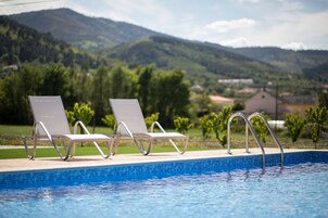 Piscina com três espreguiçadeiras brancas e escadas de metal.