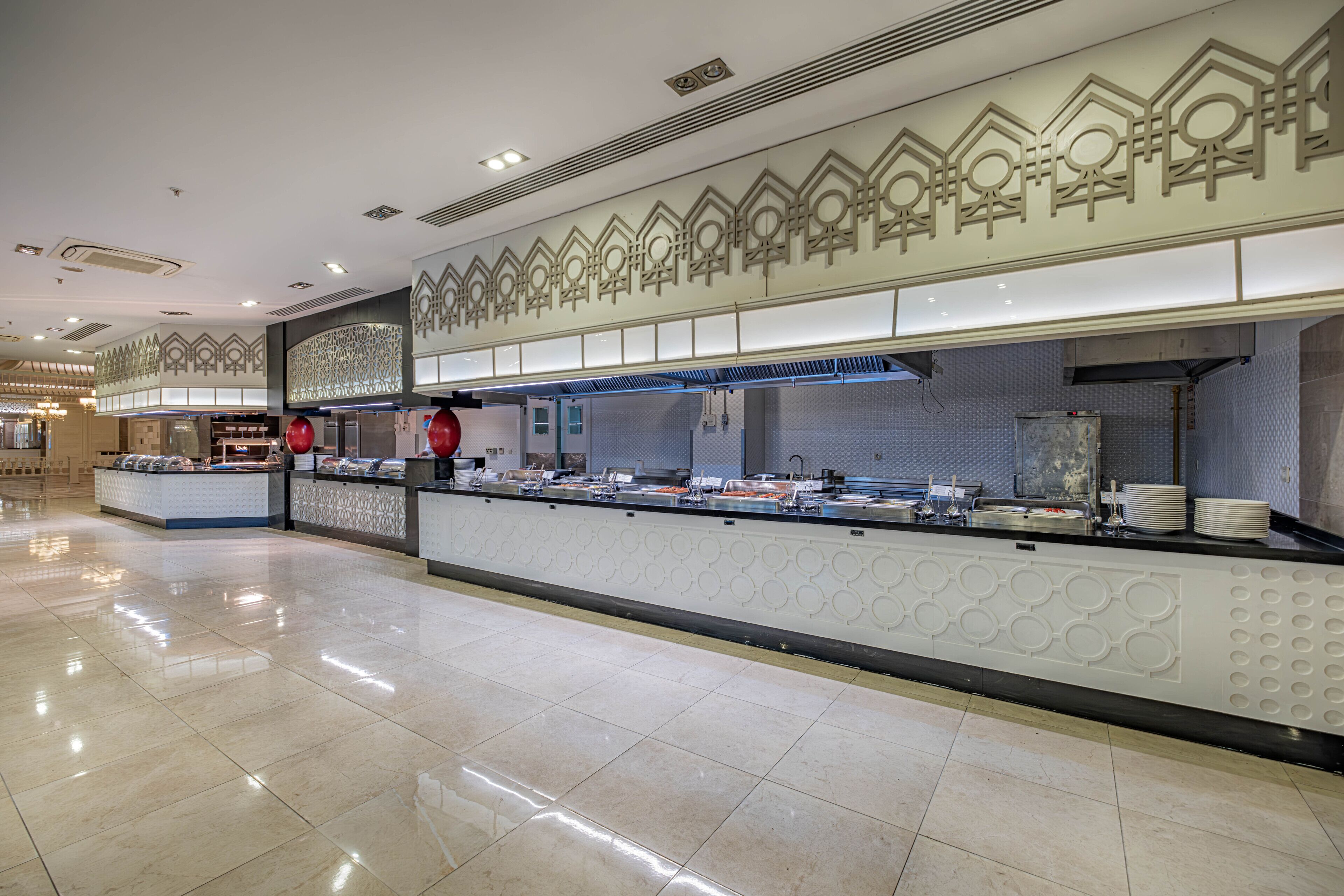 Uma área de buffet com um balcão comprido, padrões decorativos na parede e piso ladrilhado.