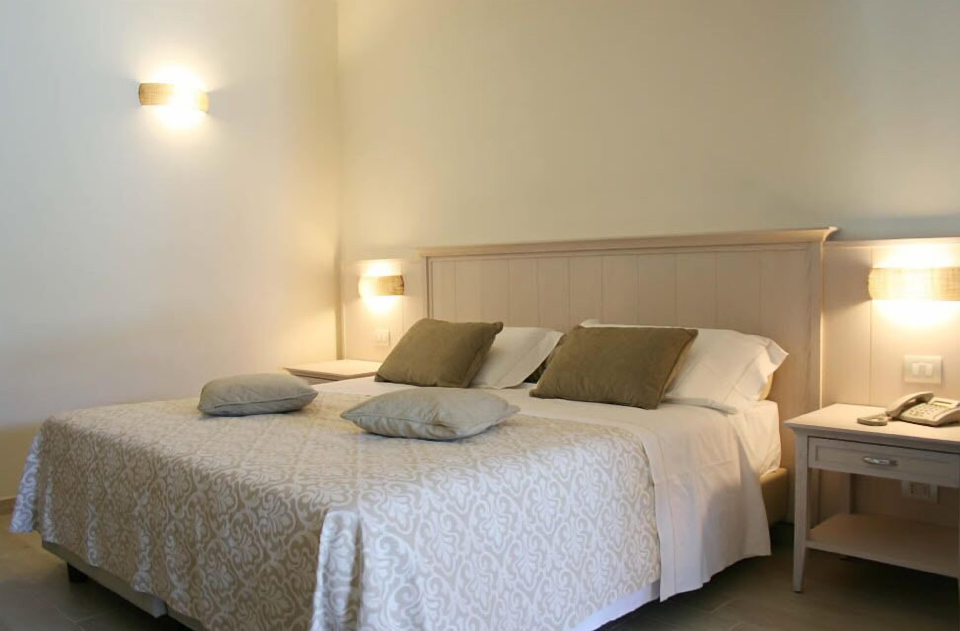Cama bem arrumada com colcha estampada, duas luminárias de cabeceira e mesa de cabeceira com telefone.