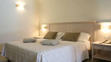 Cama bem arrumada com colcha estampada, duas luminárias de cabeceira e mesa de cabeceira com telefone.