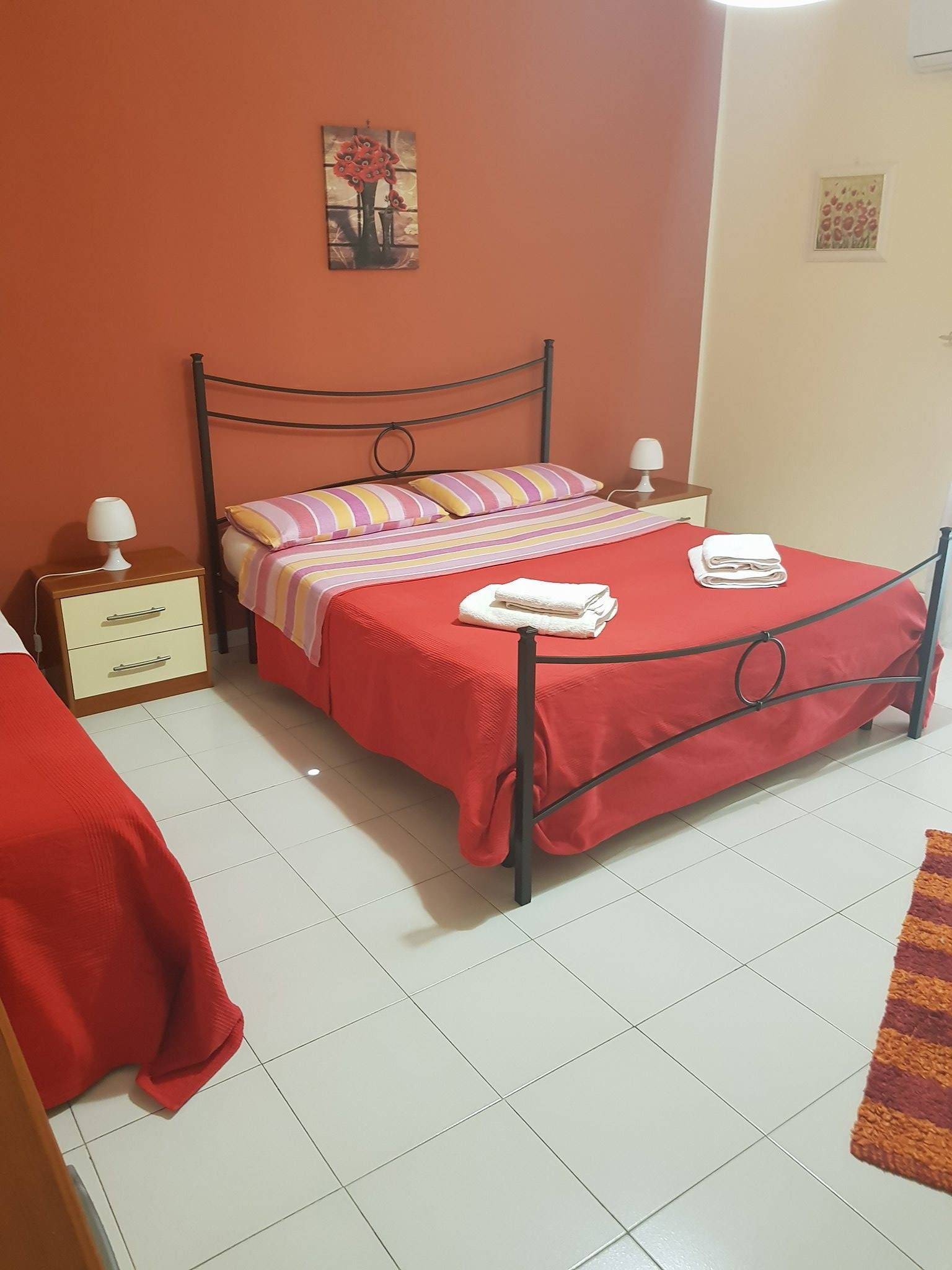 Um quarto com uma cama, mesa de cabeceira, luminária e uma pequena pintura na parede.