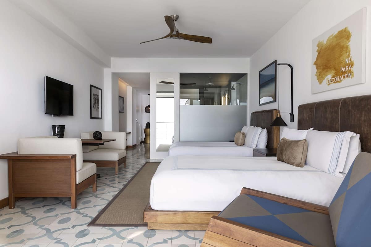 Quarto de hotel moderno com uma cama grande, um sofá, uma escrivaninha e uma televisão.