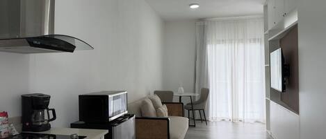 Cozinha moderna com fogão, micro-ondas e cafeteira. Há uma área de jantar com mesa e cadeiras.