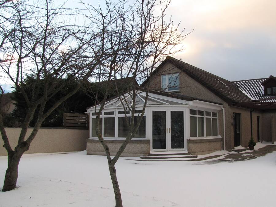 Uma casa com varanda coberta, garagem e quintal coberto de neve.